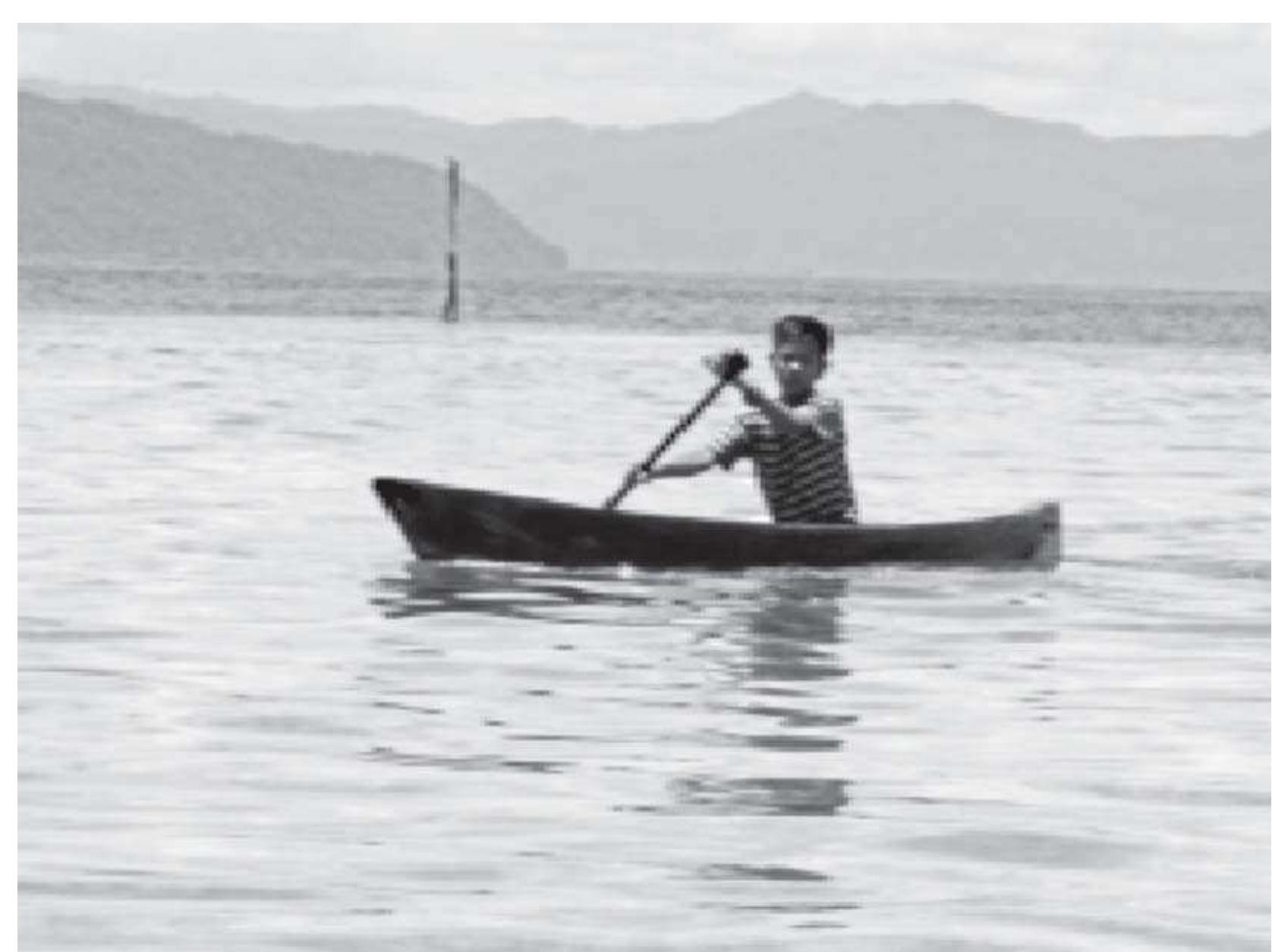 Young bajau fisher paddling a small dugout canoe, pulau